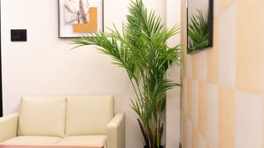 Quarto com sofá bege, uma mesinha com um controle remoto e uma planta em vaso.