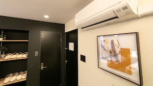 Quarto de hotel com porta preta, ar-condicionado fixado na parede e pintura abstrata emoldurada.