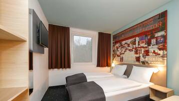 Quarto de hotel com duas camas, televisão de tela plana, janela grande com cortinas e um mural na parede.