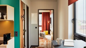 Quarto de hotel com cozinha compacta, área de jantar com mesa e cadeiras, janela com persianas e vista para a cidade.