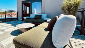 Uma área externa moderna com assentos, incluindo um sofá e cadeiras, uma mesa redonda e um vaso com planta.