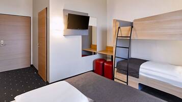 Quarto de hotel moderno com cama beliche, escrivaninha com cadeira, televisão de tela plana na parede e uma pequena área de estar com bancos.