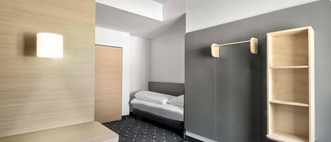 Quarto de hotel moderno com cama, um pequeno espaço de estar, prateleira na parede e um cesto de lixo.