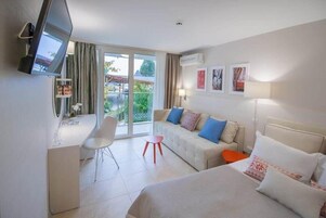 Quarto de hotel com uma cama, um sofá, uma mesa com cadeira, uma TV na parede e varanda com vista para o exterior.