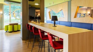 Uma área de bar moderna, com um balcão comprido, banquetas vermelhas e uma janela grande que oferece vista para o exterior.