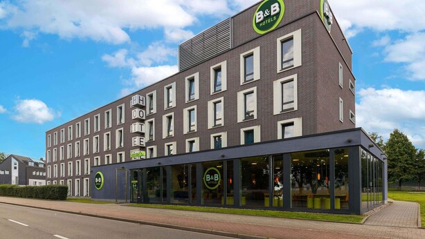 Um hotel tipo bed and breakfast com design moderno, apresentando uma área de recepção e vários quartos visíveis através de amplas janelas.