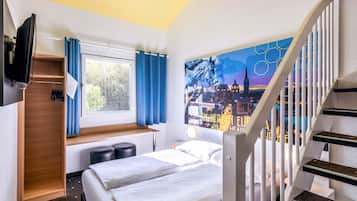 Quarto de hotel com cama, escrivaninha, janela com cortinas, um quadro na parede e uma escada.