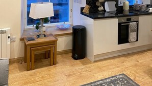 Uma cozinha moderna com janela, uma mesa pequena com luminária e uma lixeira preta.