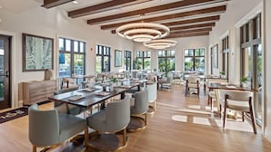 Uma sala de jantar ampla, com mesas e cadeiras compridas, janelas grandes e um design de teto moderno.