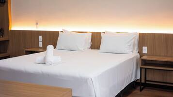 Quarto de hotel com uma cama grande, duas mesas de cabeceira e uma luminária fixada na parede.
