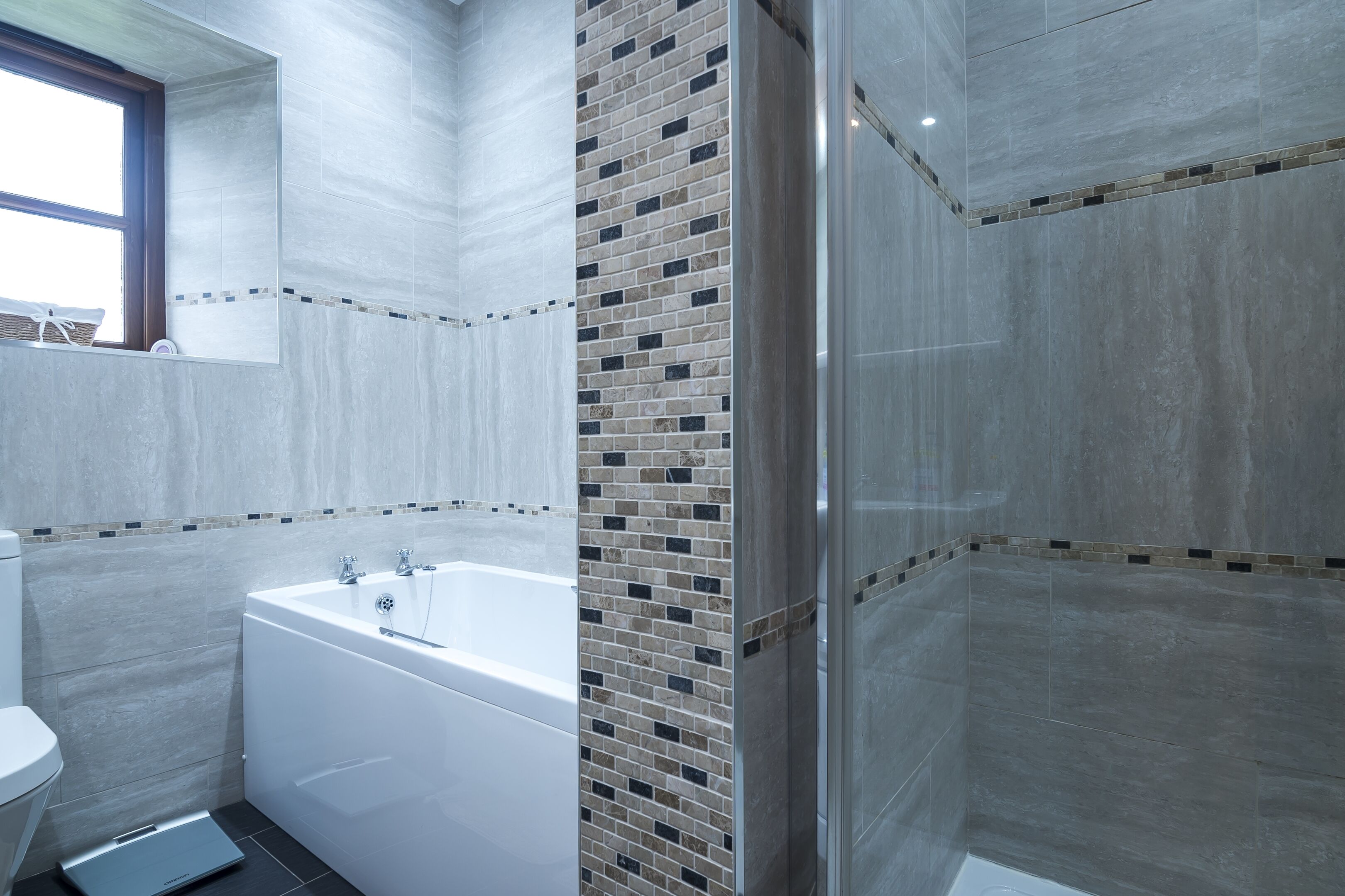 Um banheiro moderno com uma banheira branca, box de vidro e painel de azulejos.