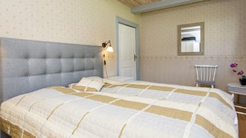 Quarto com uma cama grande, mesa de cabeceira, cadeira, luminária na parede e uma porta.