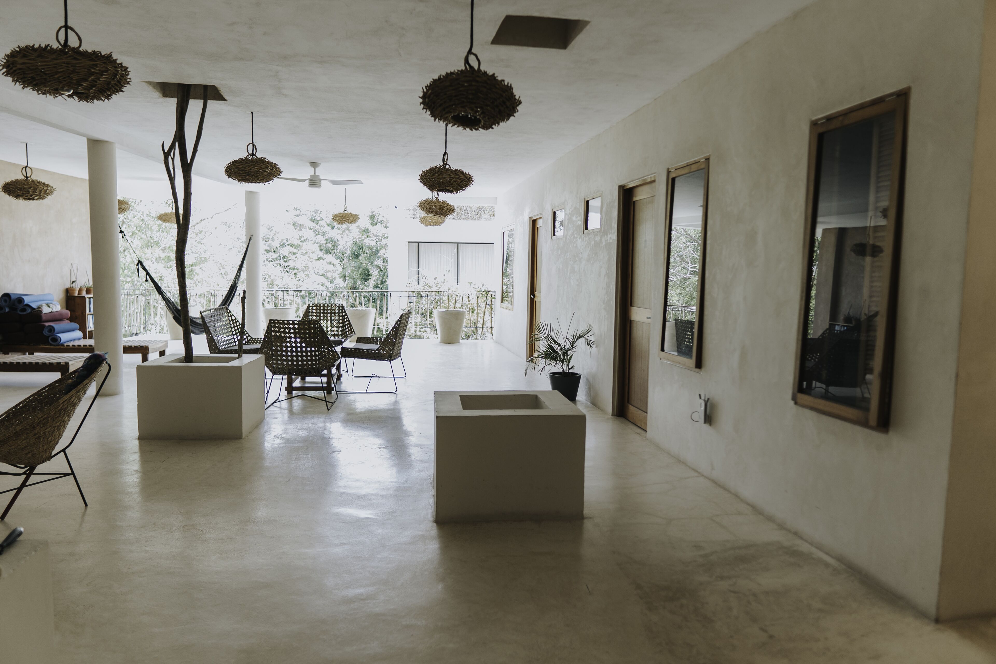 Um interior espaçoso e moderno com design minimalista, apresentando uma área de estar central com cadeiras e uma rede, tudo envolto por amplas janelas e luminárias esféricas penduradas.