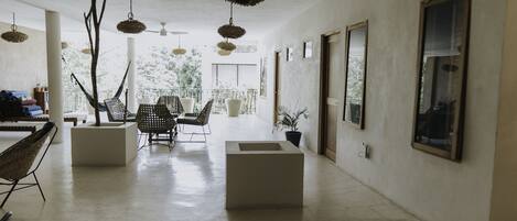 Um interior espaçoso e moderno com design minimalista, apresentando uma área de estar central com cadeiras e uma rede, tudo envolto por amplas janelas e luminárias esféricas penduradas.