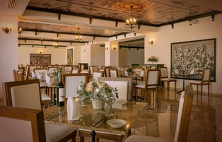Uma sala de jantar com várias mesas preparadas para hóspedes, com mesas de mármore polido, cadeiras de madeira e elegantes louças, incluindo copos de vinho e arranjos florais.