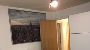 Quarto com vista para a cidade, porta de madeira, penteadeira branca e colcha estampada.