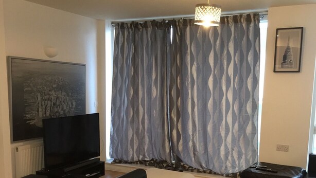Uma sala de estar moderna com uma TV de tela plana, sofás de couro preto, uma cortina estampada e um quadro na parede.