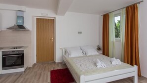 Um quarto com cama, tapete vermelho, porta de madeira e janela com cortinas.