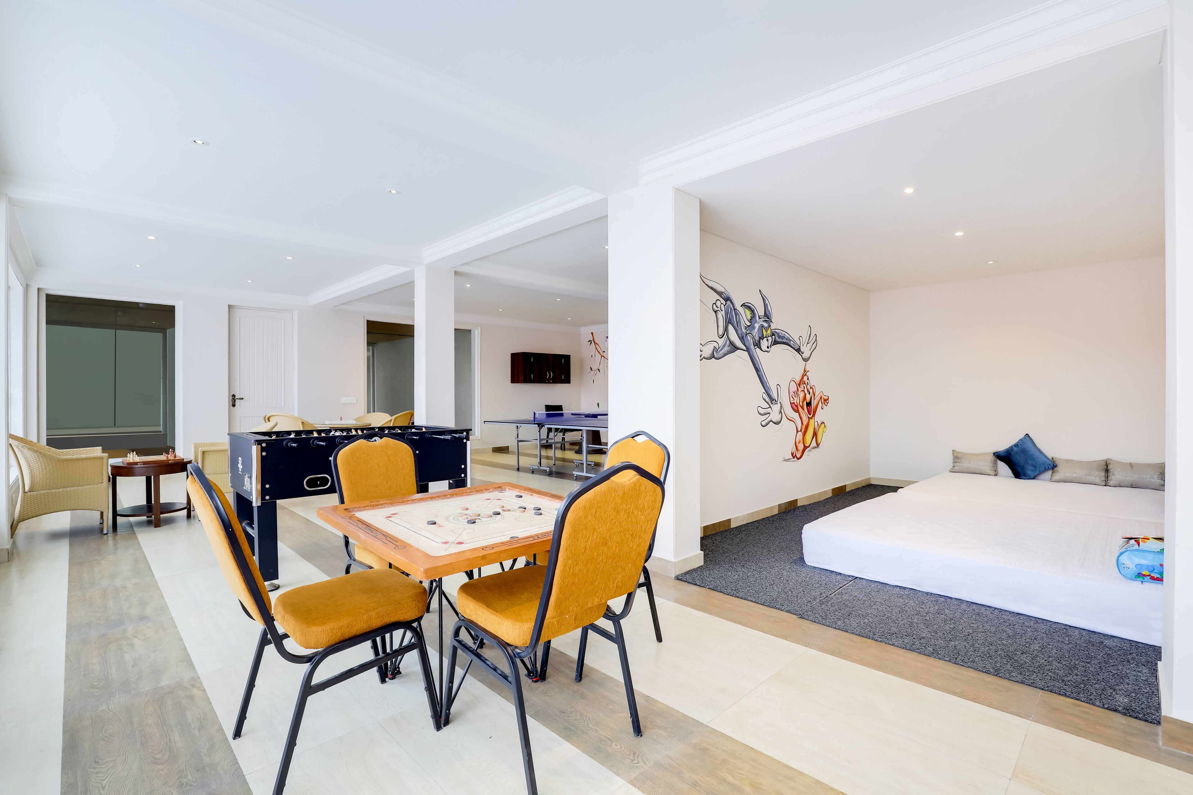 Quarto de hotel com cama, mesa de pebolim e área de refeições com cadeiras e mesa.