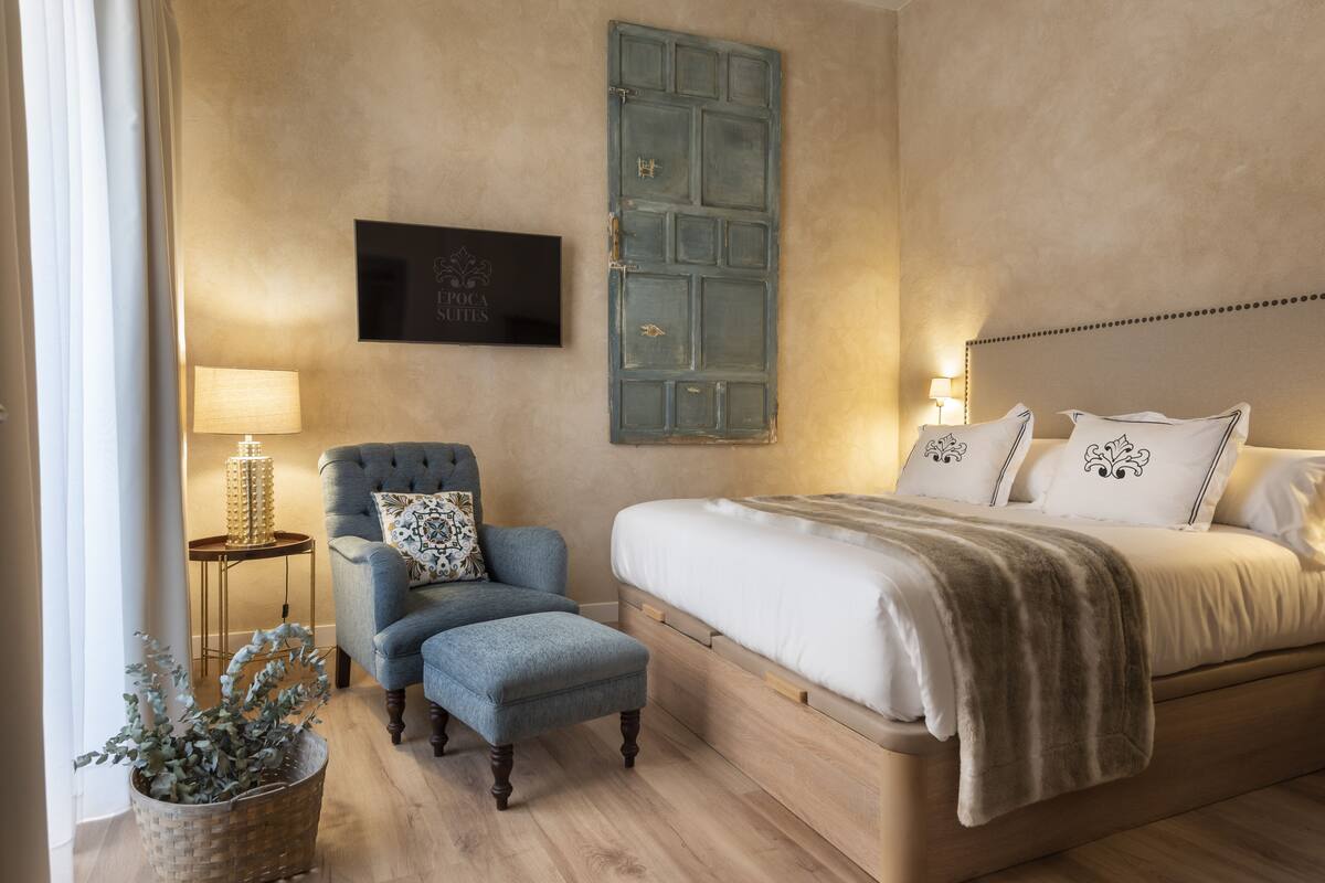 Quarto com cama, cadeira, televisão fixada na parede e painel decorativo na parede.