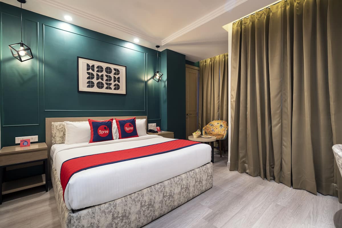 Quarto de hotel com uma cama grande, duas mesas de cabeceira, um criado-mudo, uma obra de arte emoldurada na parede e uma janela com cortinas.