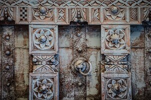 Uma porta de madeira desgastada pelo tempo, com delicados entalhes florais e detalhes em metal.