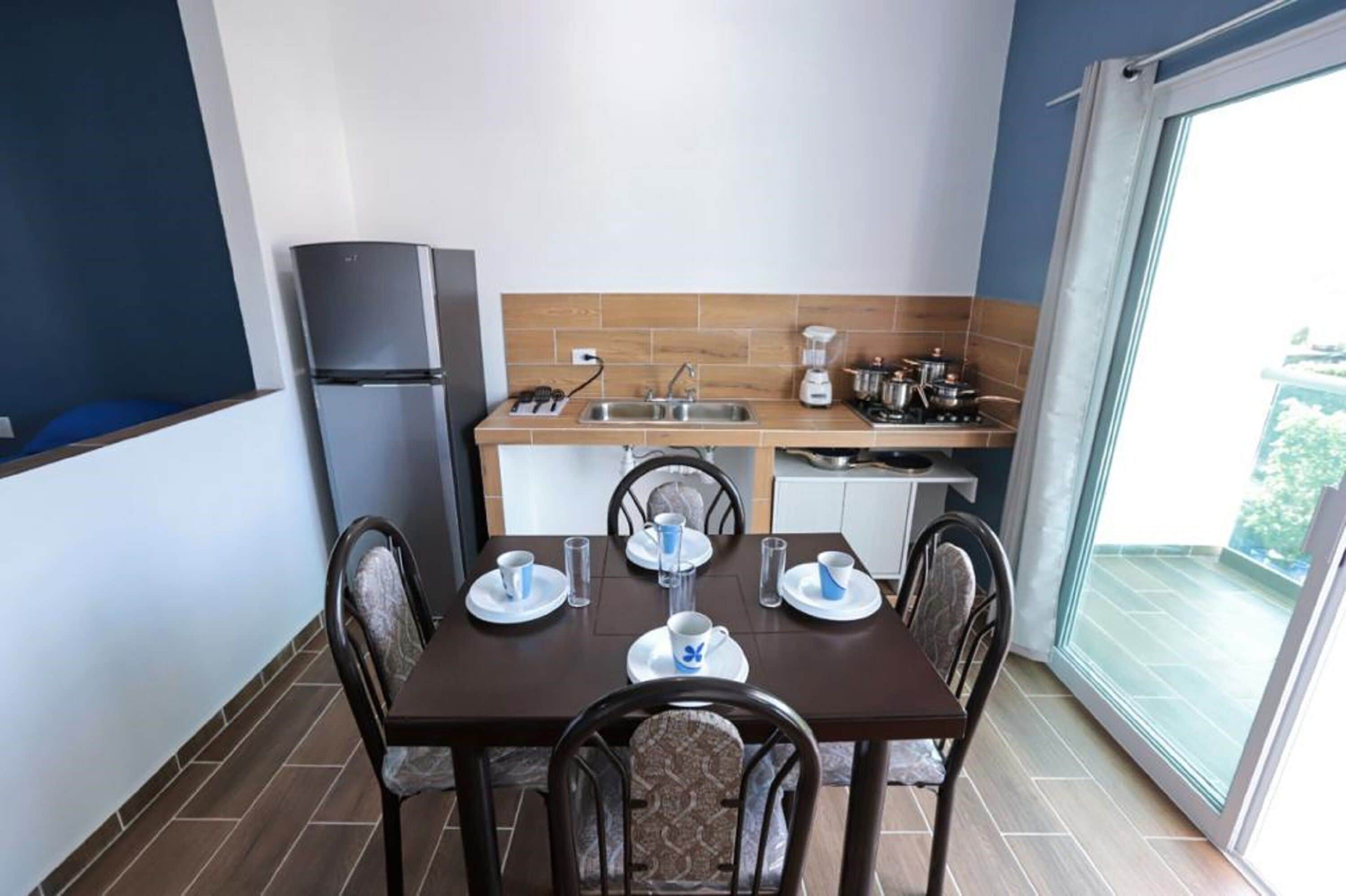 Cozinha compacta com mesa de jantar posta para quatro, geladeira e vista para o exterior.