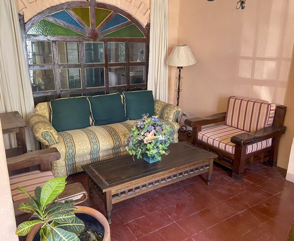 Uma sala de estar acolhedora com um sofá estampado, uma poltrona listrada, uma mesa de centro de madeira e uma planta em vaso.