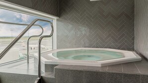 Casa de banho moderna com uma banheira grande, vista para um aeroporto e parede com padrão herringbone.