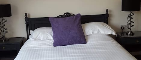 Uma cama bem arrumada com lençóis brancos, um travesseiro roxo e duas toalhas brancas dobradas sobre a cama.