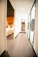 Quarto de hotel moderno com cabeceira de madeira, cama com almofadas amarelas, um espelho grande e uma porta deslizante.