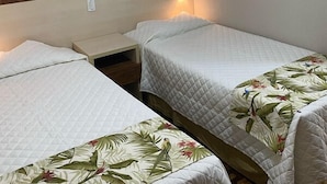 Quarto pequeno e limpo com duas camas de solteiro, uma mesinha de cabeceira, ventilador de teto e ar condicionado na parede.