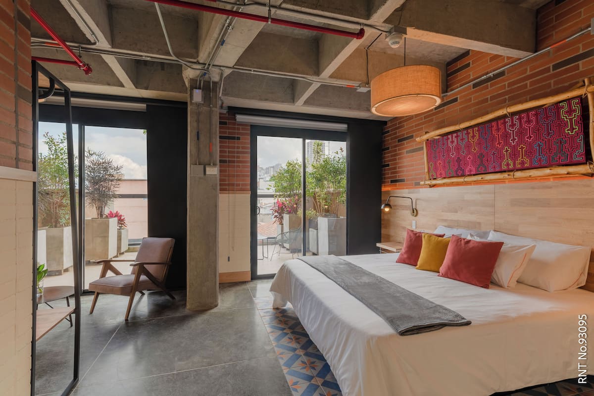 Quarto de hotel moderno com uma cama grande, uma poltrona e vista para o exterior.