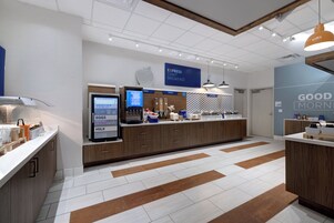 Espaço de café da manhã moderno com estação de autoatendimento, painel de menu digital e parede com a mensagem 'Bom dia'.