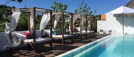 Uma área à beira da piscina com espreguiçadeiras e uma cobertura.