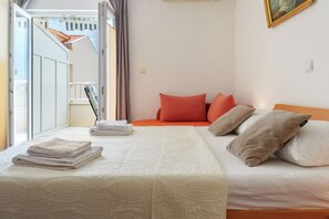 Quarto com cama, almofadas, toalha dobrada, janela e um quadro na parede.