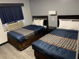 Quarto de hotel com duas camas, janela com cortinas, ar-condicionado e luminária fixada na parede.