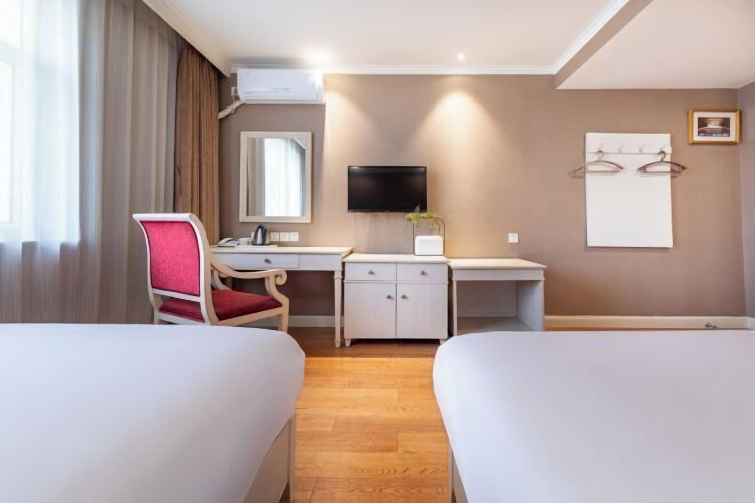 Quarto de hotel com duas camas, uma escrivaninha com cadeira, uma televisão e um espelho.