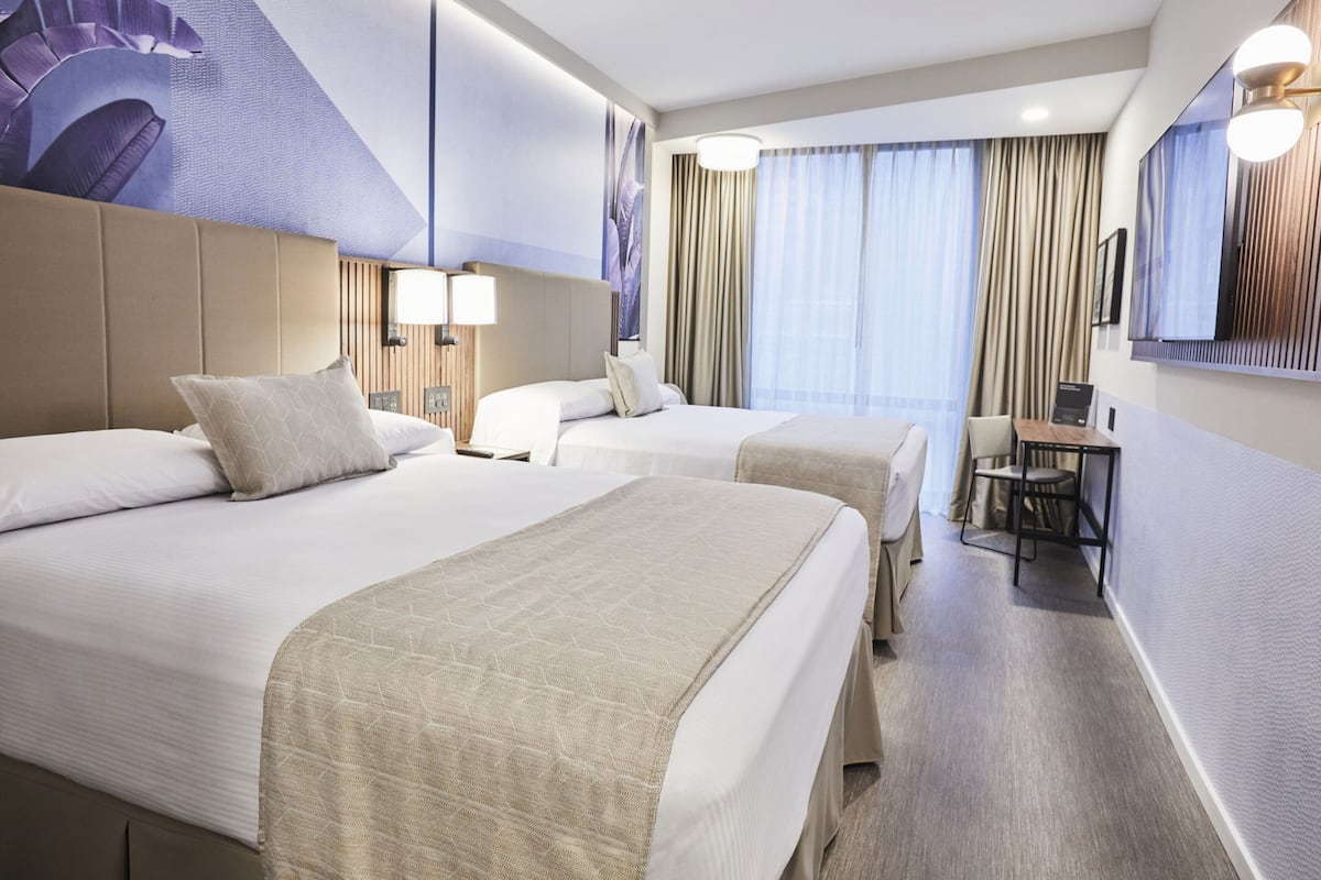 Quarto de hotel com duas camas, uma mesa e uma cadeira.