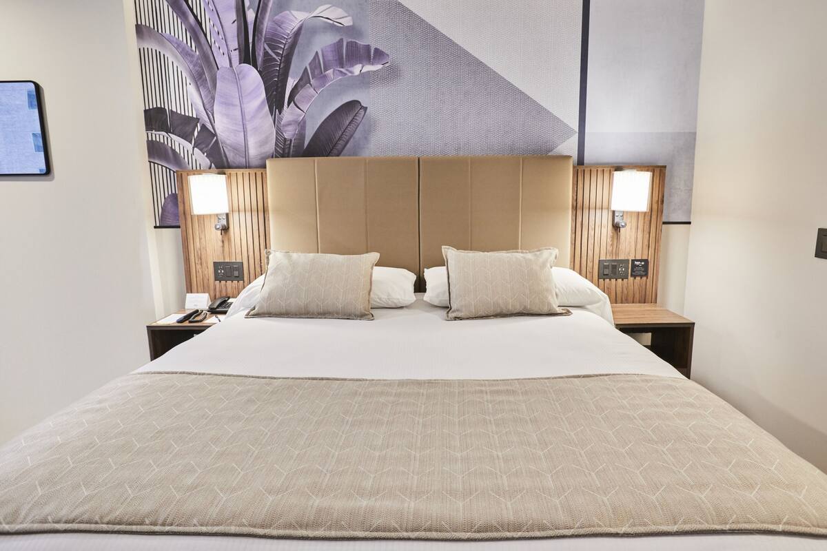 Quarto de hotel com uma cama grande, duas mesas de cabeceira, uma cabeceira e uma obra de arte pendurada na parede.