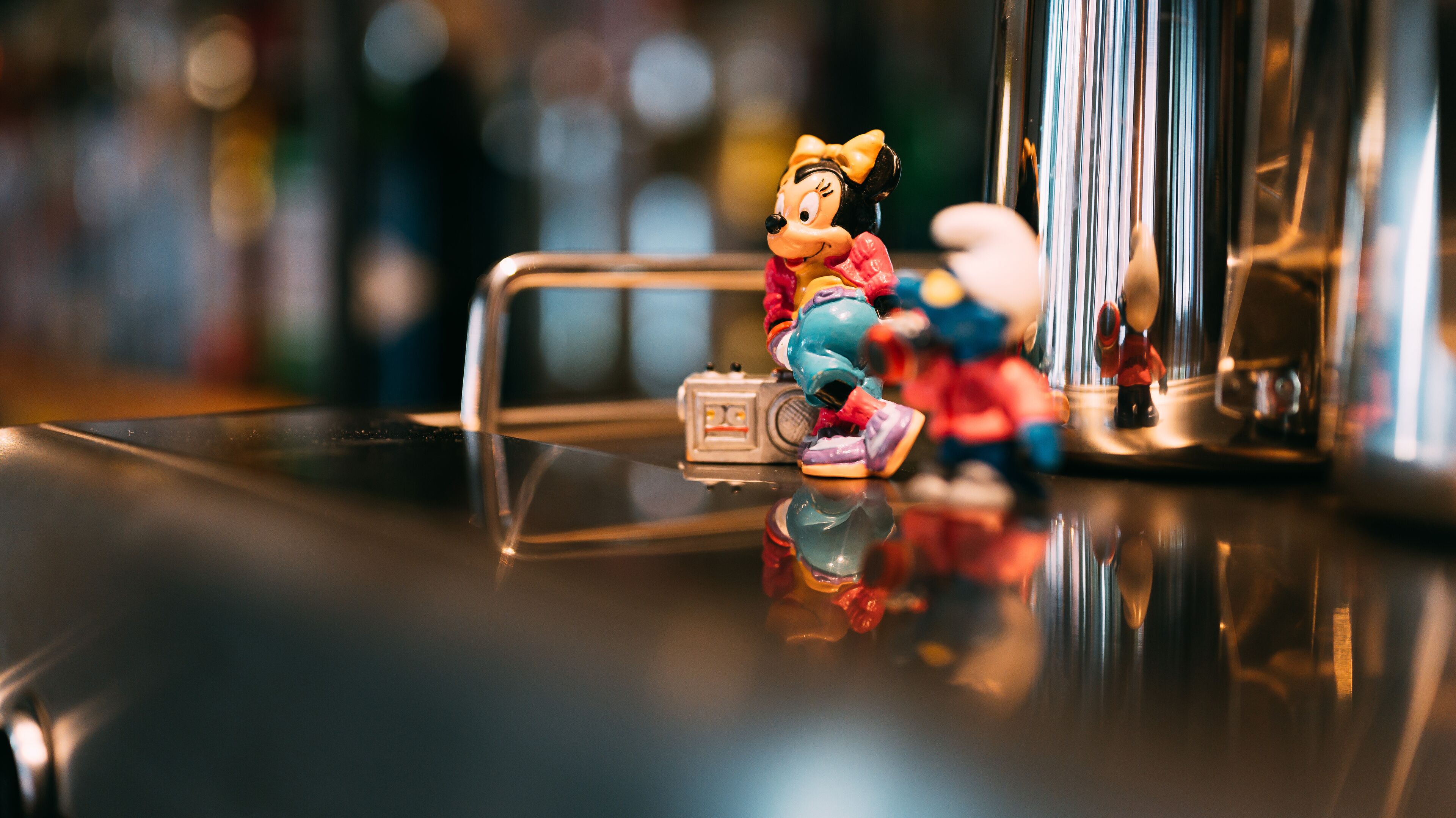 Uma figura de um personagem com um arco, um rádio e um pequeno carrinho de brinquedo sobre uma superfície espelhada.