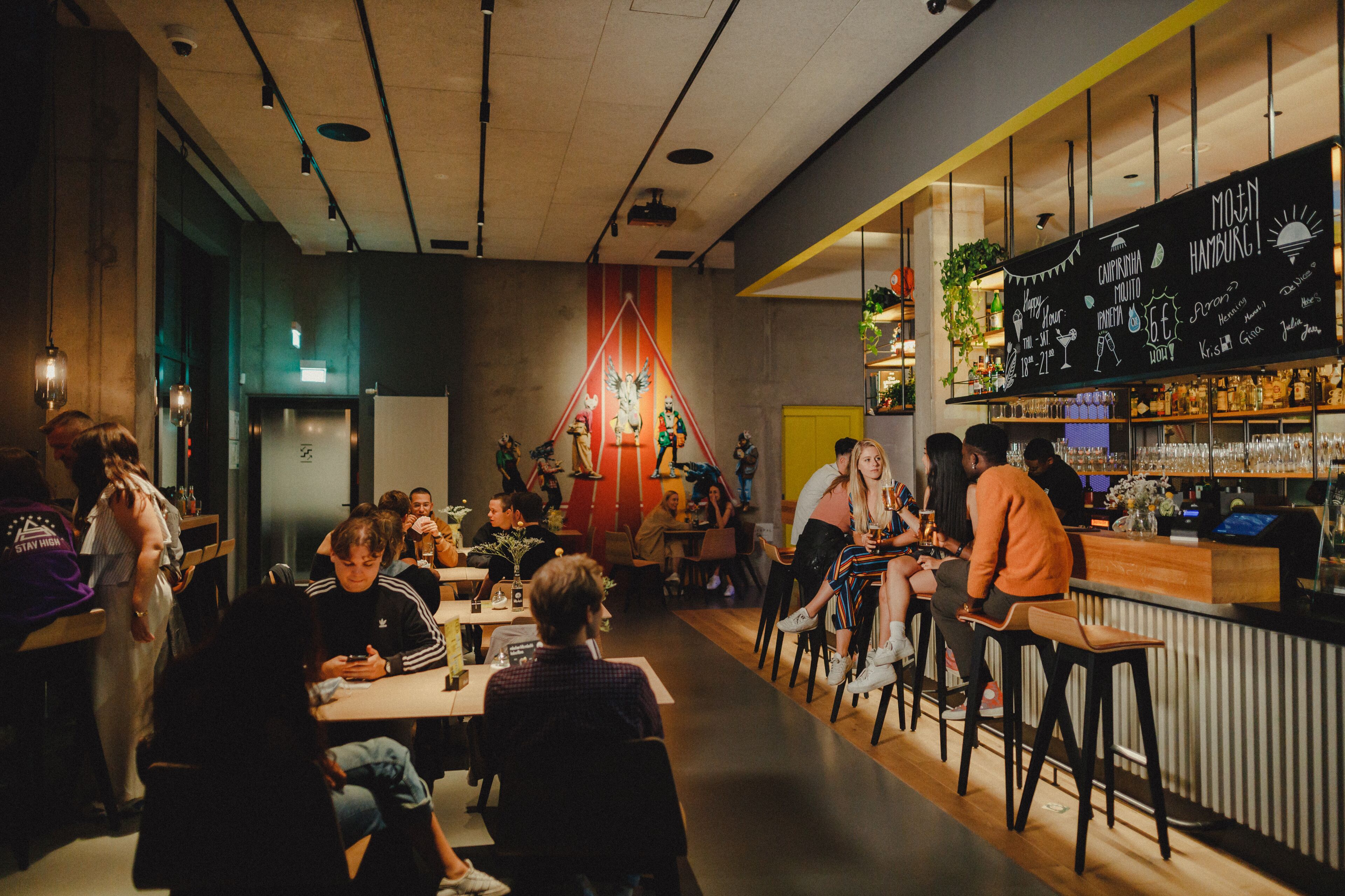 Uma área de bar com cardápio em lousa, assentos e parede decorativa.