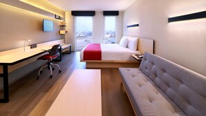 Quarto de hotel moderno com escrivaninha, cadeira, cama e sofá.