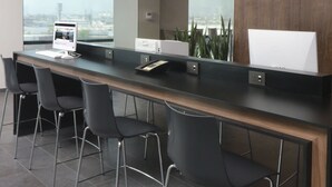 Uma área de bar moderna com um balcão comprido, três cadeiras pretas e uma grande janela com vista para a cidade.