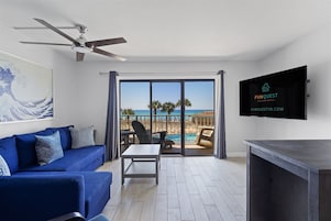 Quarto moderno com sofá azul, uma mesinha, ventoinha no teto e uma televisão exibindo 'FUNQUEST Vacation Rentals'.