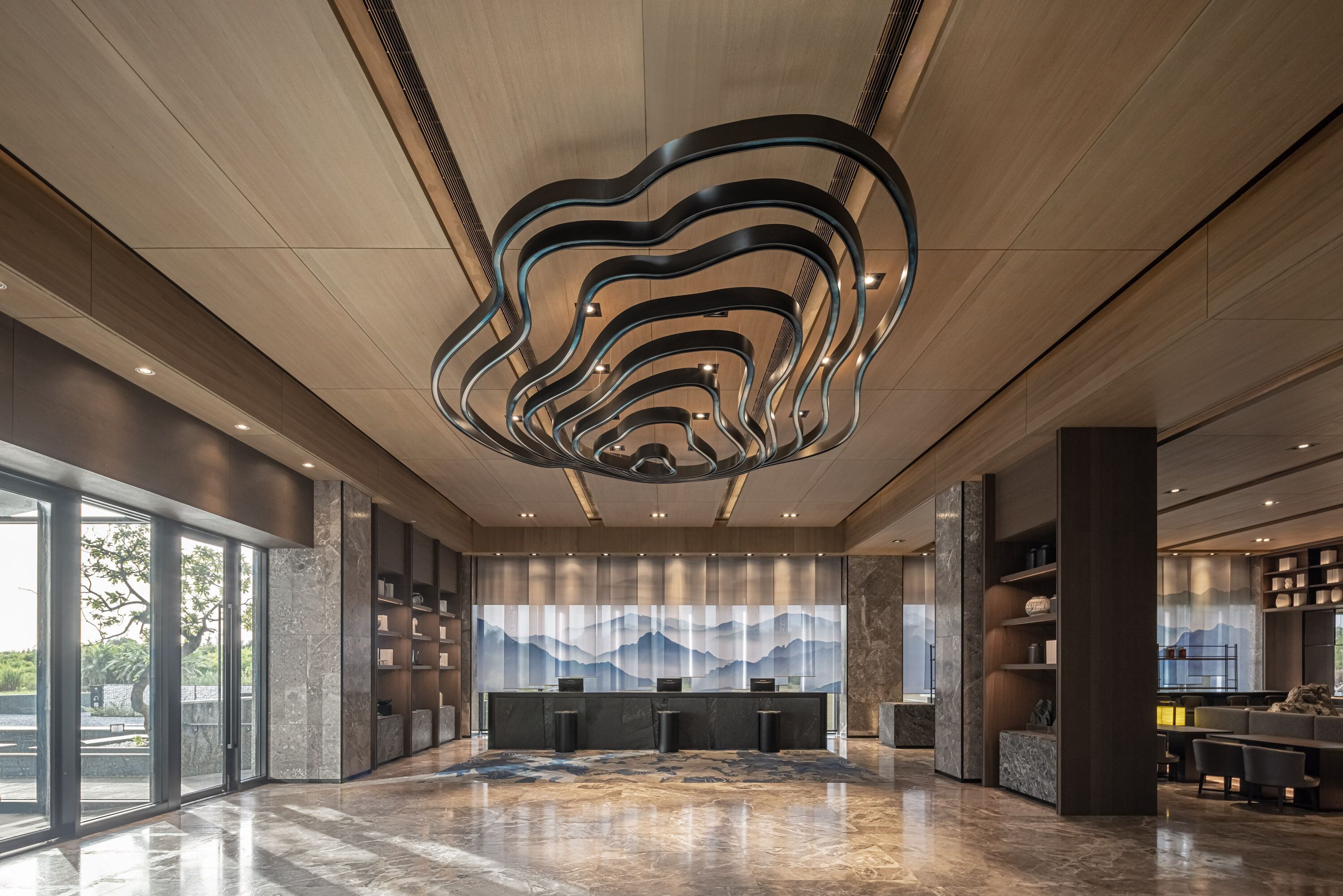 Um hall amplo com design moderno, apresentando uma escultura de teto única, um balcão de recepção e uma grande janela com vista para as montanhas.