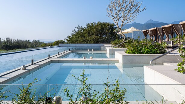 Piscina moderna ao ar livre com água cristalina, ladeada por degraus e vegetação, com vista para uma paisagem montanhosa.