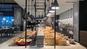 Interior de restaurante moderno com um balcão extenso, diversas mesas para refeições e uma variedade de pratos expostos.