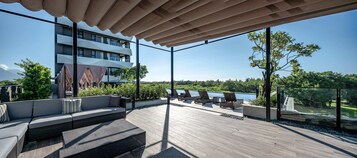 Um deck moderno ao ar livre com sofá, poltronas de descanso e vista para um lago e montanhas.