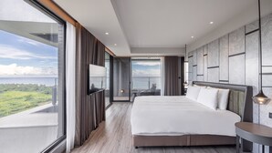 Quarto de hotel moderno com uma cama grande, uma TV e uma varanda com vista para o mar.